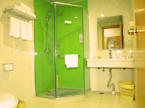 Um banheiro com box verde, pia branca com espelho acima e uma cesta amarela.