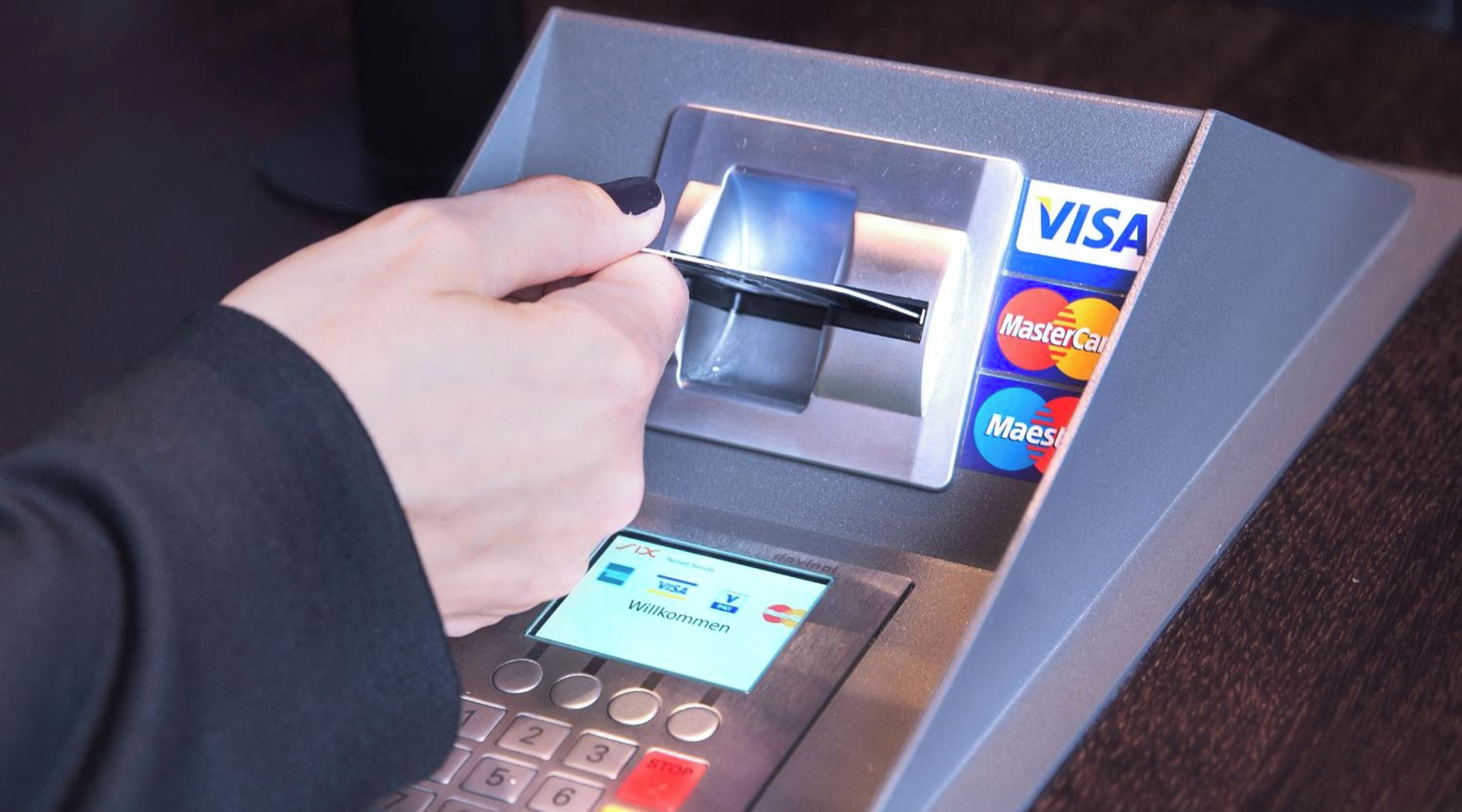Mão inserindo cartão em terminal de pagamento, com logotipos Visa e MasterCard.