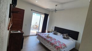 Quarto com cama, escrivaninha, ventoinha no teto e vista para o exterior.