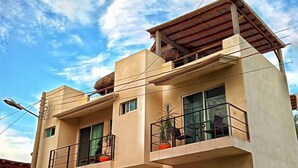 Um edifício de dois andares com telhado plano, janelas amplas e uma varanda com mobiliário de exterior.