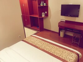 Quarto de hotel com cama, televisão, escrivaninha e guarda-roupa.