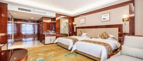 Quarto de hotel com duas camas, área de estar, mesa de trabalho e banheiro.