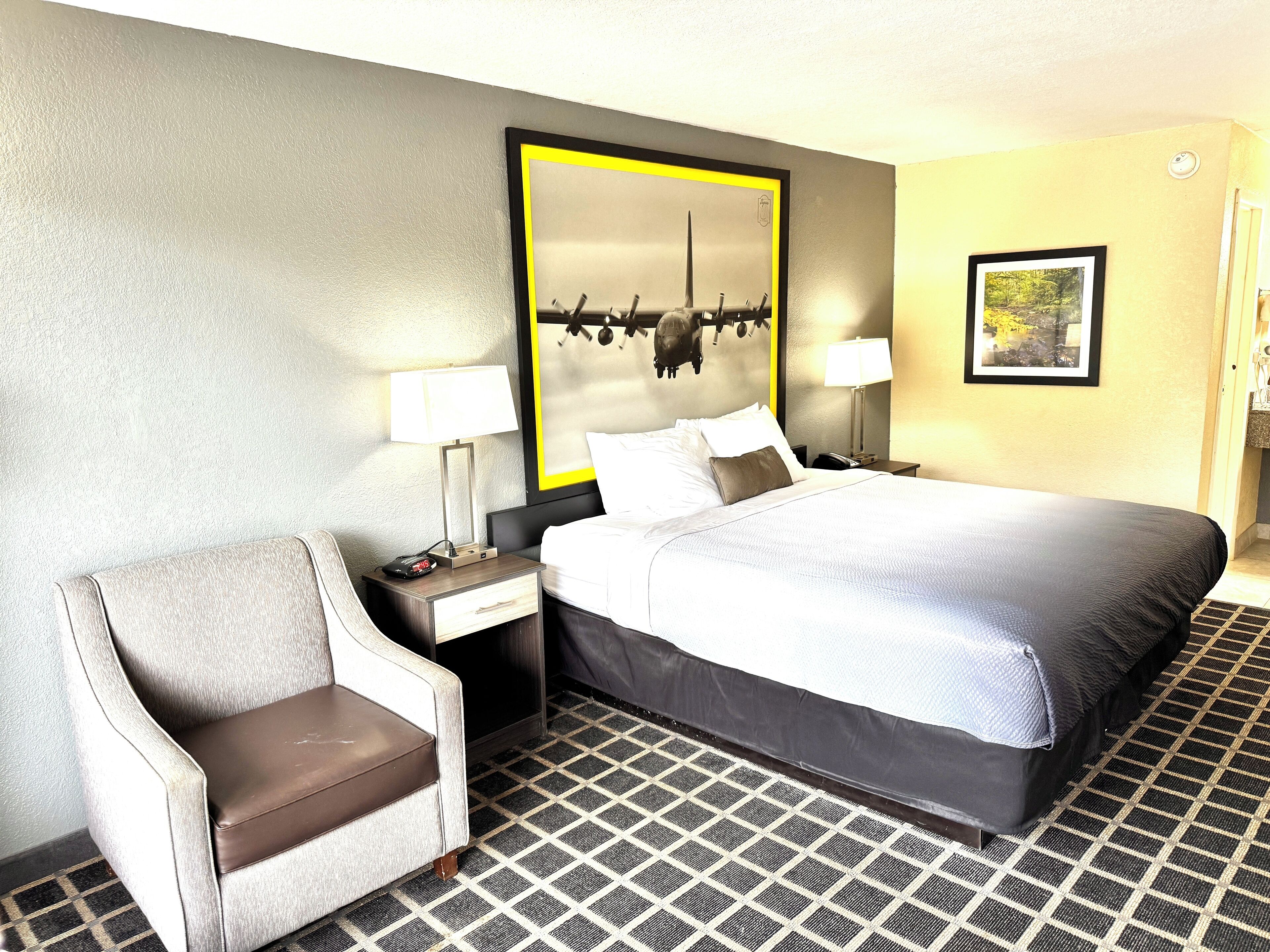 Quarto de hotel com cama, duas mesas de cabeceira com luminárias, uma cadeira e um espelho grande na parede.