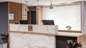 Balcão de recepção de hotel com bancada de mármore, painel de parede de madeira e três lustres.