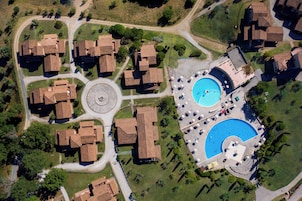 Vista aérea de um bairro residencial com várias casas, um acesso circular e uma piscina com espreguiçadeiras.