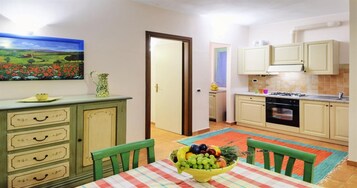 Uma cozinha com uma mesa de jantar, cadeiras, uma fruteira e um quadro na parede.
