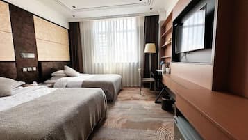 Quarto de hotel com duas camas, televisão, escrivaninha e uma janela grande com cortinas.