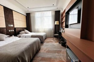Quarto de hotel com duas camas, televisão, escrivaninha e uma janela grande com cortinas.