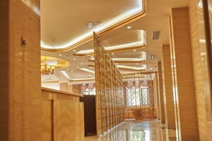Um hall de hotel luxuoso com design moderno, apresentando um piso refletante, iluminação elegante e um painel decorativo.