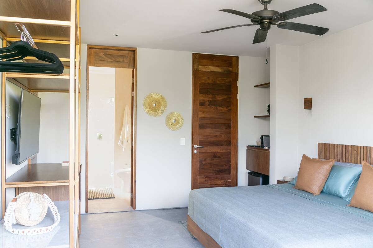 Quarto com cama, ventoinha no teto, guarda-roupa e porta que dá para outro cômodo.