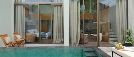 Quarto de hotel moderno com porta de vidro que dá para uma varanda, piscina e área de refeições com mesas ao ar livre.