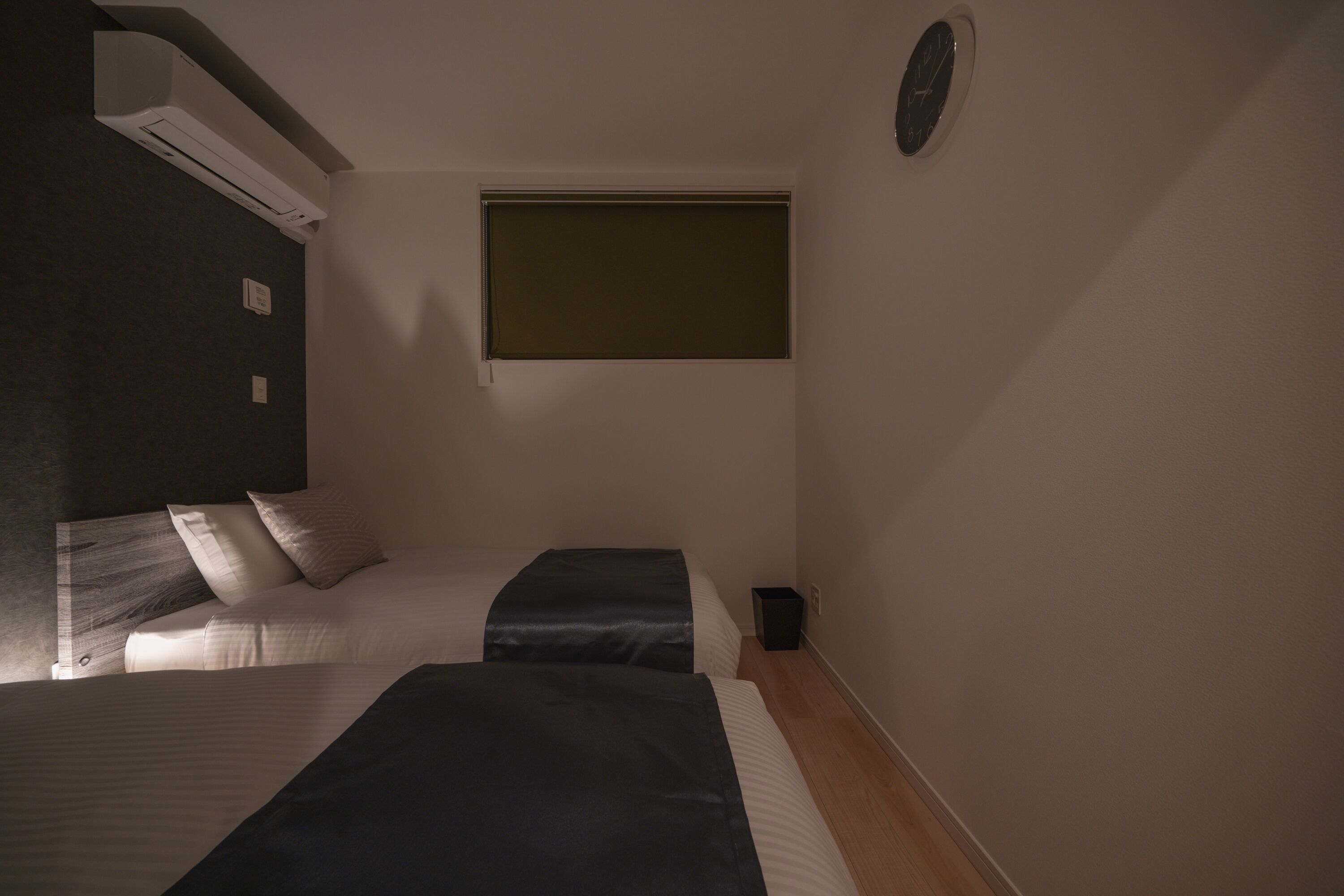 Quarto com duas camas, uma janela e relógio fixado na parede.