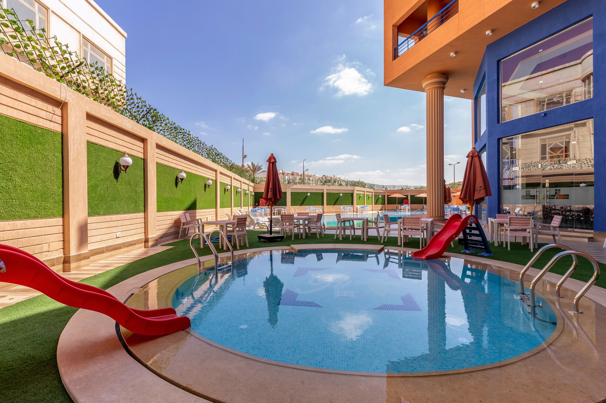 Uma área de piscina com escorregador, cadeiras de sol e guarda-sóis.