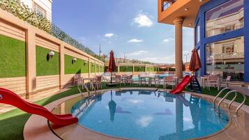 Uma área de piscina com escorregador, cadeiras de sol e guarda-sóis.