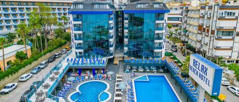 Um hotel com uma piscina grande, várias varandas e vista para montanhas.