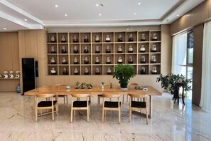 Uma área de refeições com uma mesa de madeira comprida e cadeiras, uma parede decorada com objetos e uma planta grande.