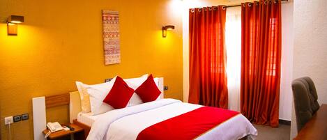 Quarto de hotel com cama, escrivaninha, telefone e ar condicionado fixado na parede.