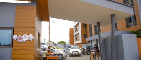 Entrada de hotel com um letreiro, área de estacionamento coberta e uma pessoa numa motocicleta.