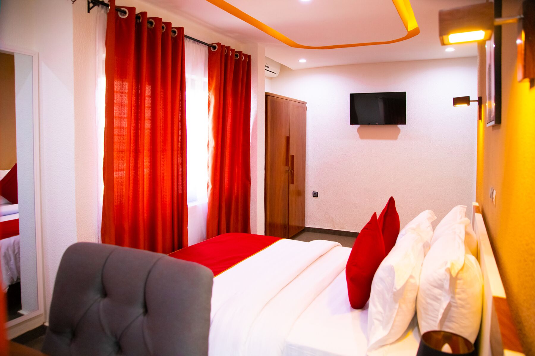 Quarto de hotel com uma cama, uma cadeira, televisão na parede e uma porta.
