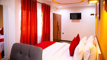 Quarto de hotel com uma cama, uma cadeira, televisão na parede e uma porta.