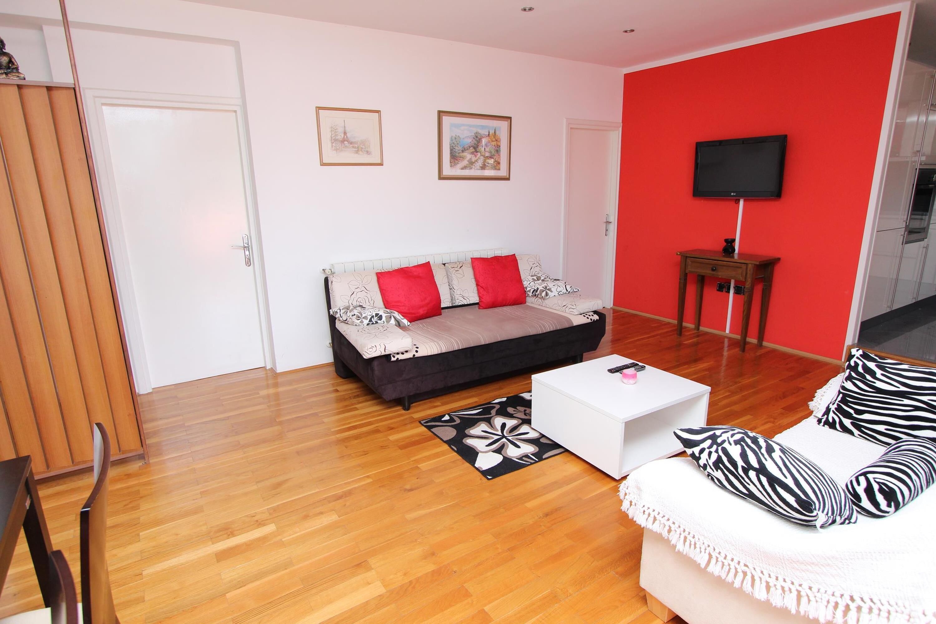 Uma sala de estar com sofá, mesa de centro, televisão e uma parede vermelha de destaque.