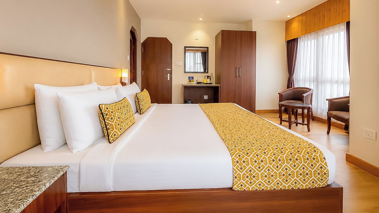 Quarto de hotel com cama grande, escrivaninha, cadeira, guarda-roupa e espelho.
