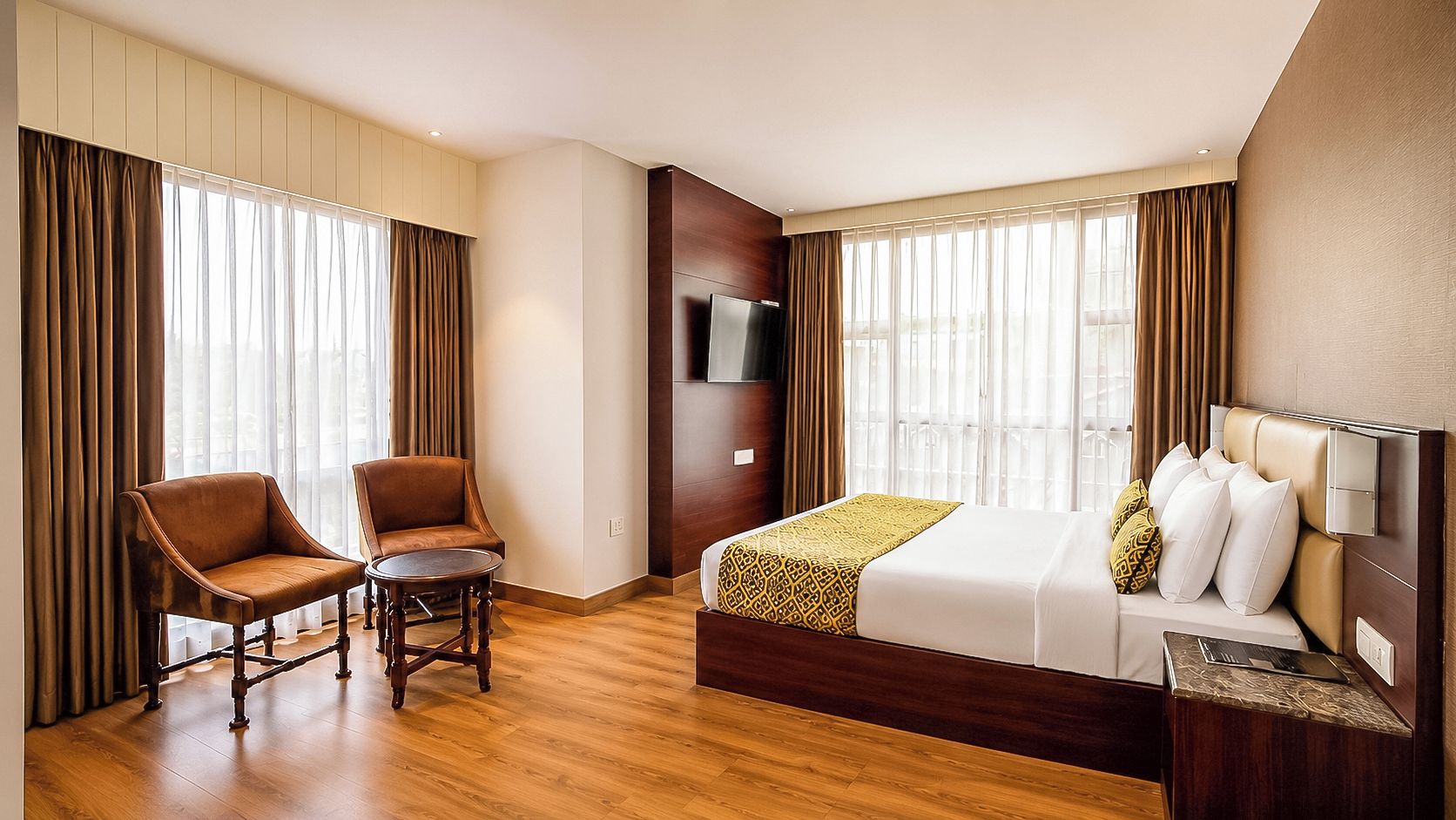Quarto de hotel com uma cama, uma cadeira, uma mesinha e uma televisão.