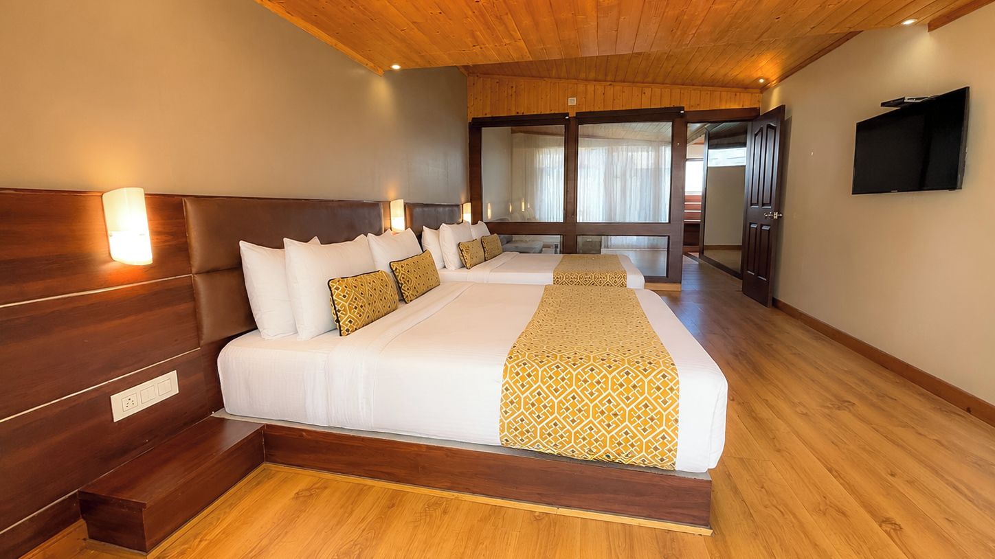 Quarto de hotel com cama grande, cabeceira de madeira, luminárias laterais e televisão de tela plana.