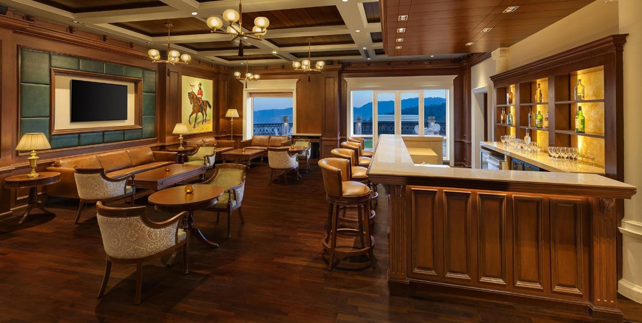 Uma área de bar com balcão extenso e banquetas, uma área de estar com sofás e mesas, e uma janela grande com vista.