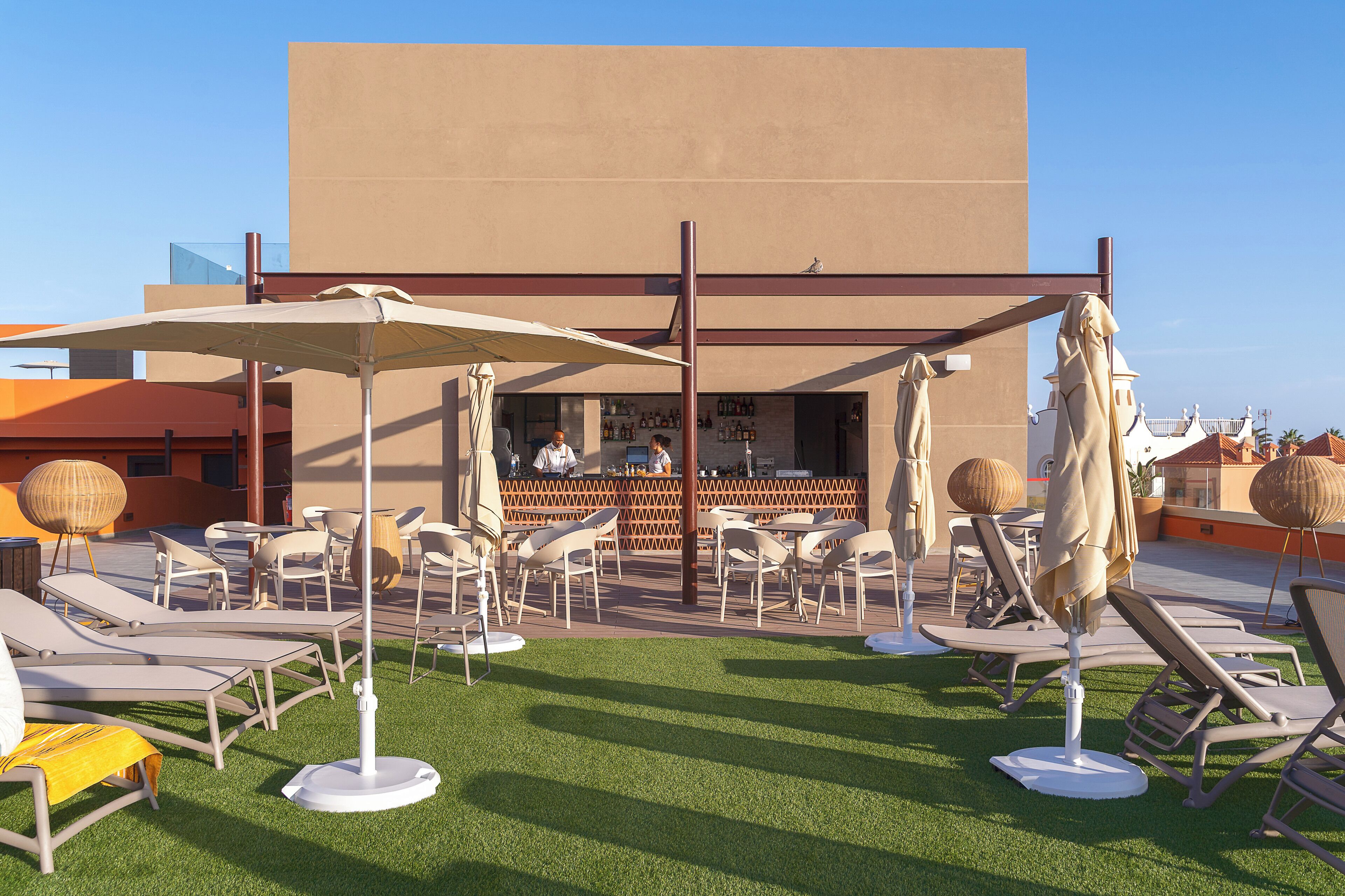 Um bar no terraço com área externa, incluindo espreguiçadeiras e guarda-sóis, e um balcão com vista para a paisagem urbana.