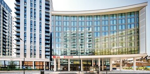 Um hotel moderno com fachada de vidro curva, várias varandas e entrada destacada com a placa ibis hotel e adagio.