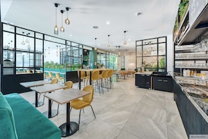 Restaurante moderno com pé-direito alto, iluminação pendente e uma combinação de assentos amarelos e verdes.