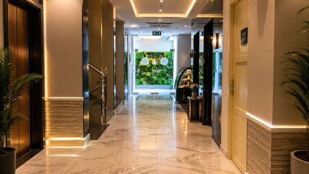 Um saguão de hotel com piso de mármore, balcão de recepção e parede verde com plantas.