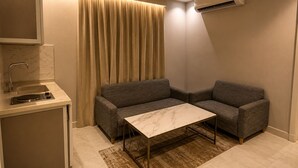 Um espaço compacto com cozinha compacta, dois sofás cinzentos, uma mesa de centro de mármore e uma cortina bege.