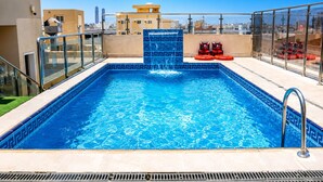 Uma piscina no terraço com borda de mosaico azul, um elemento aquático e vista para a paisagem urbana.