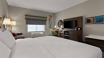 Quarto de hotel com uma cama grande, uma escrivaninha com cadeira, televisão e janela com persianas.