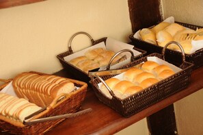 Três cestos de vime repletos de diferentes tipos de pão sobre uma prateleira de madeira.