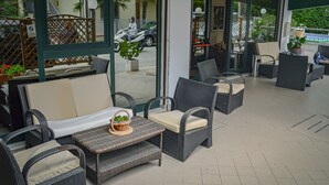 Área de estar ao ar livre coberta, com móveis de vime e uma mesa com uma planta.