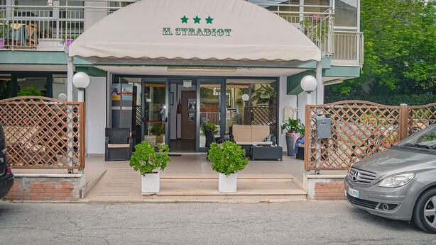 Entrada de hotel com varanda coberta, placa com três estrelas e um carro estacionado nas proximidades.