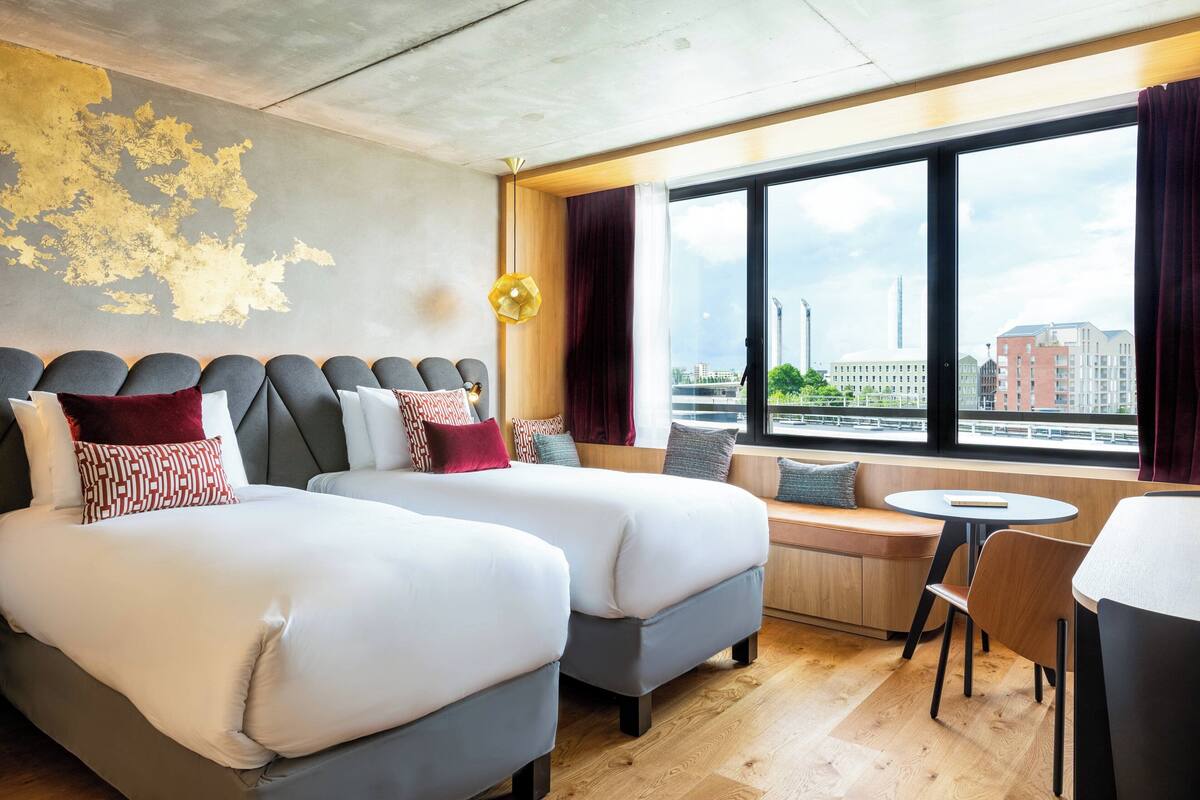 Quarto de hotel com duas camas, uma mesa pequena e vista para a cidade.