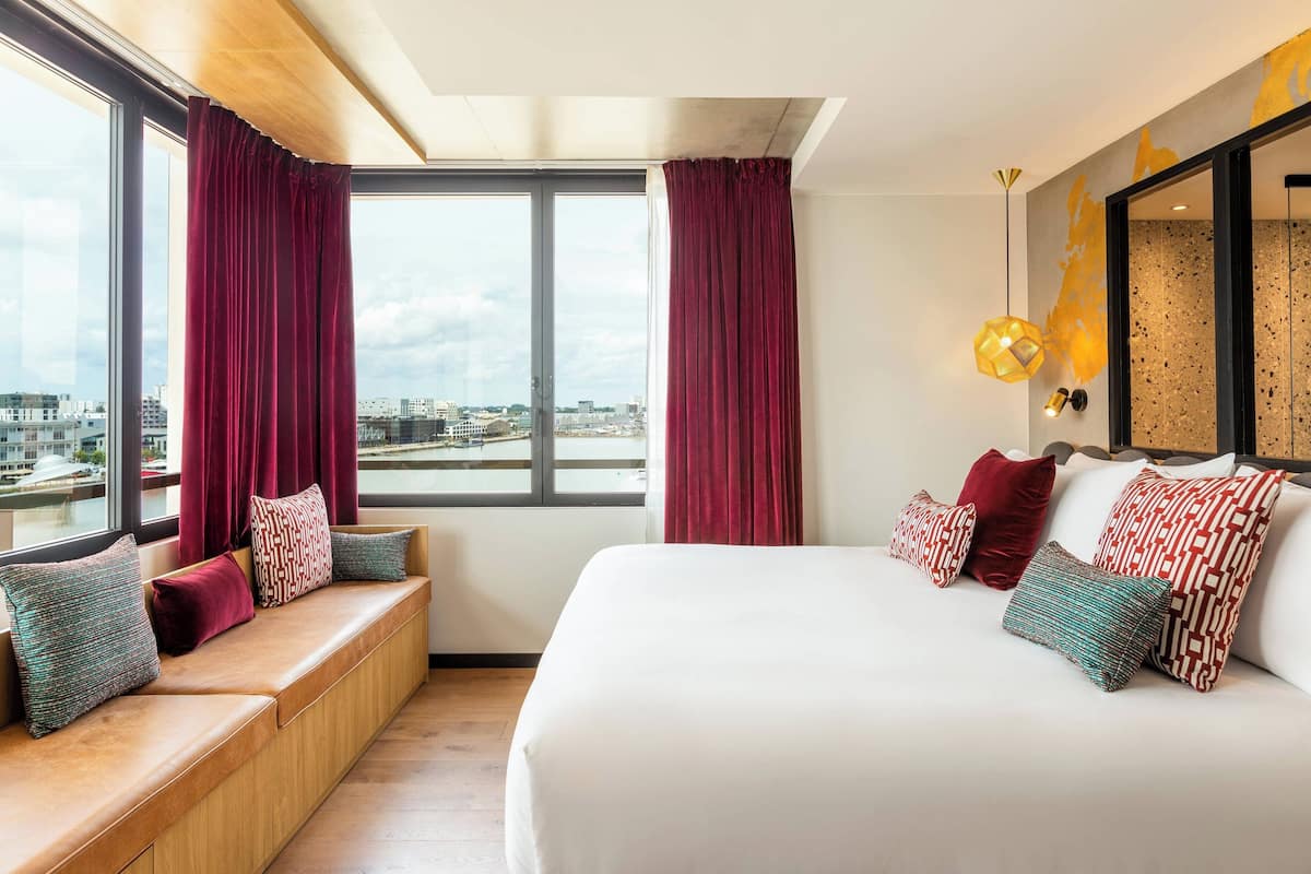 Quarto de hotel moderno com cama grande, área de estar com almofadas, vista para a cidade e design de parede único.