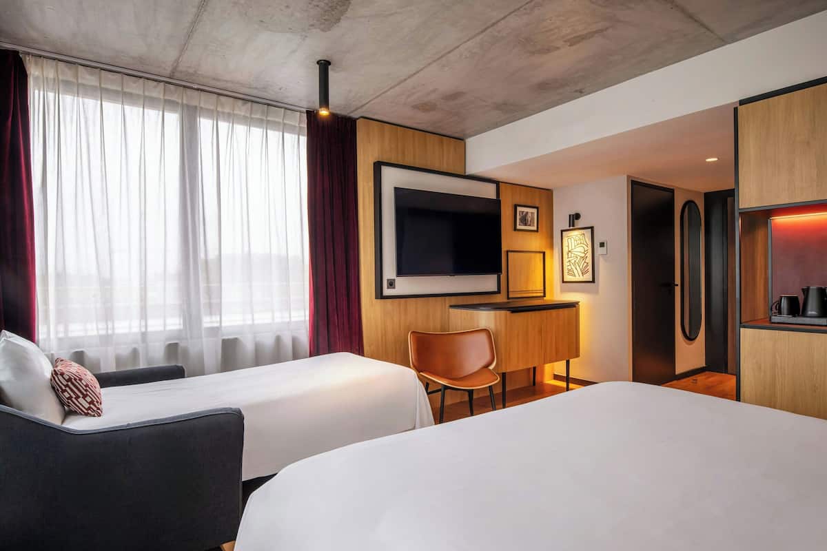Quarto de hotel com duas camas, uma escrivaninha, uma cadeira, uma televisão e um minibar.