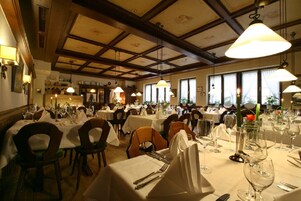 Restaurante com várias mesas postas para refeições, apresentando um interior clássico com vigas de madeira e lustres.