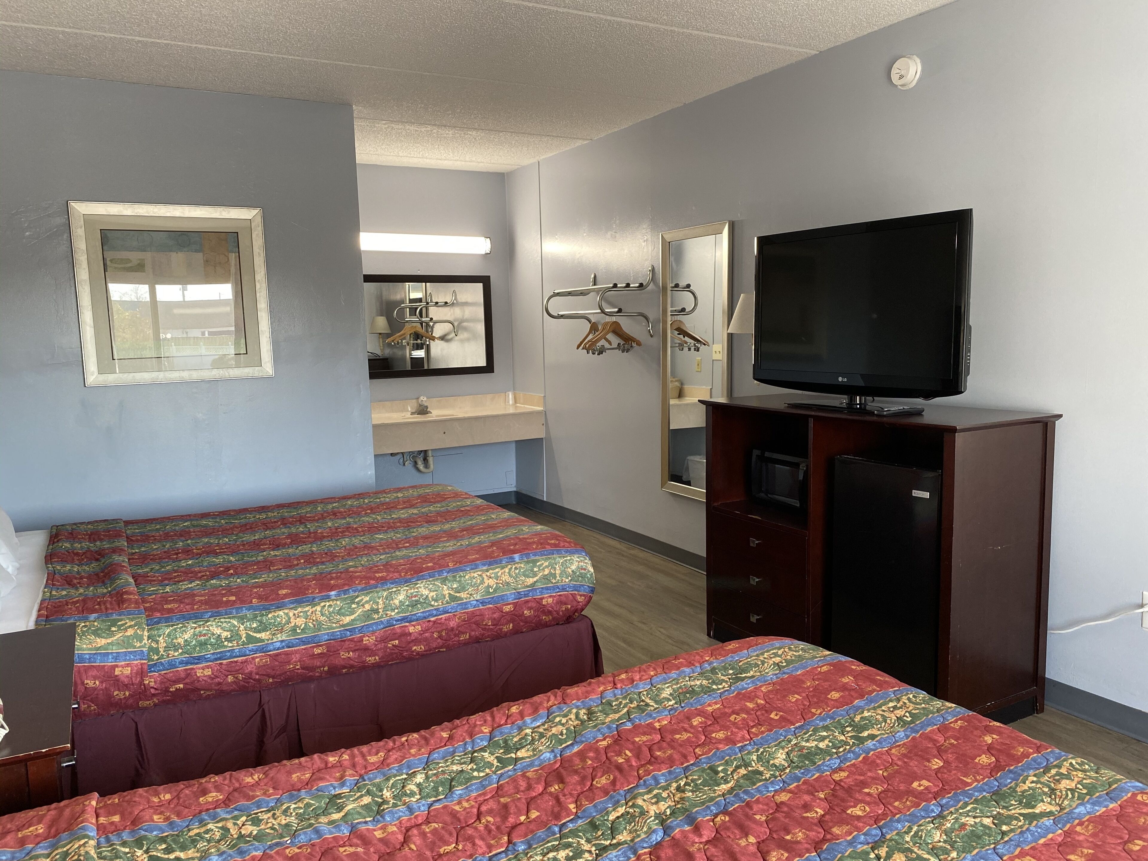 Quarto de hotel com duas camas, televisão, espelho, pia e armário.