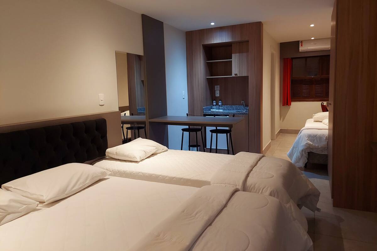 Quarto de hotel com duas camas, uma escrivaninha e uma kitchenette.