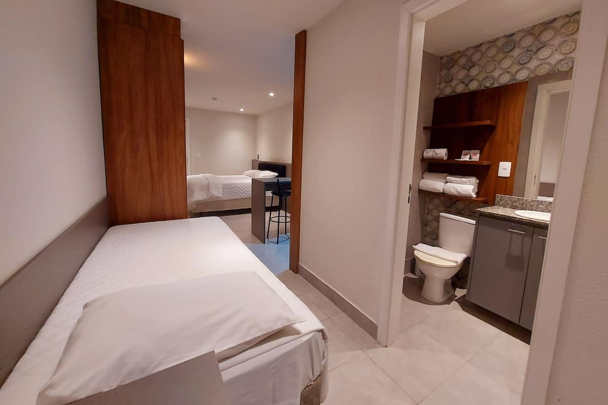 Quarto de hotel com cama, escrivaninha e banheiro com vaso sanitário e pia.
