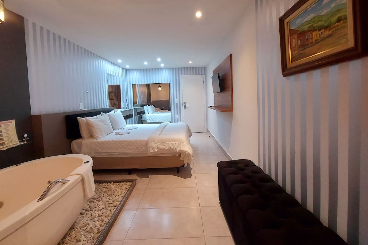 Quarto de hotel com duas camas, um espelho grande, uma TV fixada na parede e um quadro.