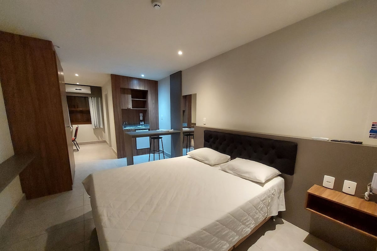 Quarto de hotel moderno com uma cama grande, uma escrivaninha pequena e uma cozinha compacta.