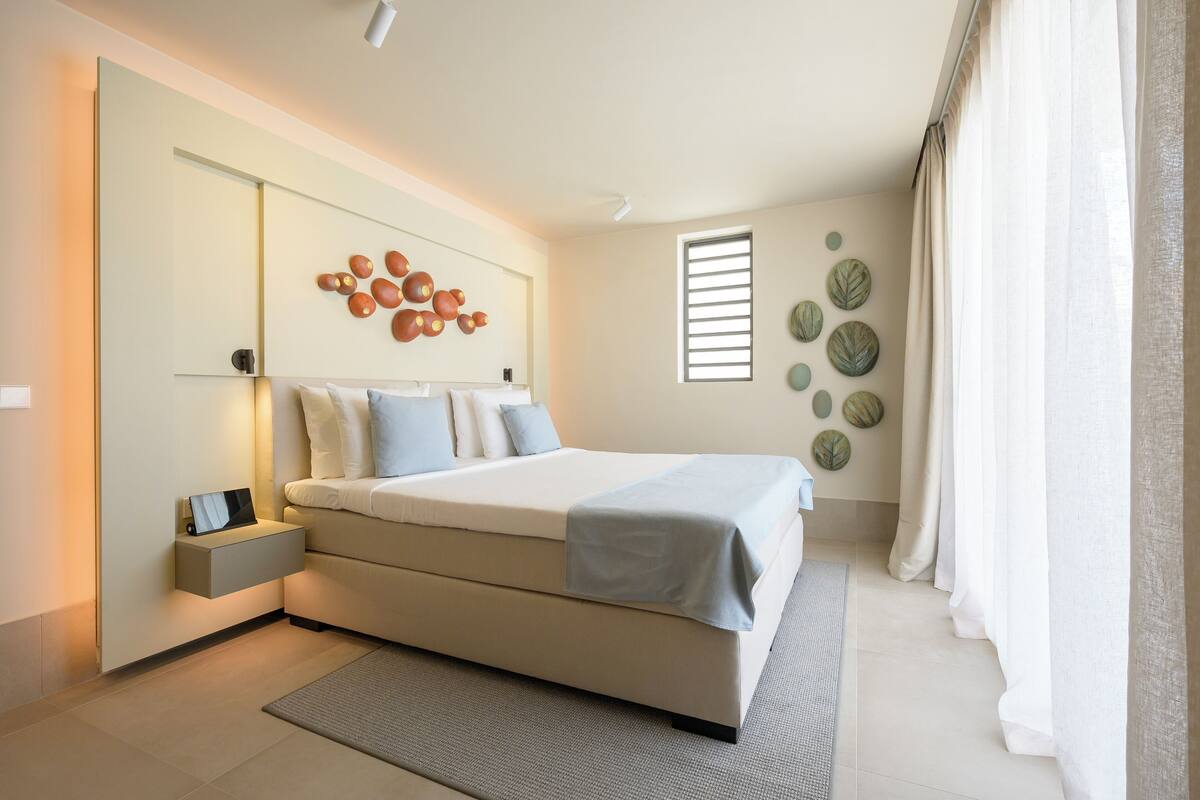 Quarto moderno com uma cama grande, mesas de cabeceira, luminária fixada na parede e arte decorativa.