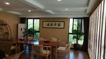 Uma área de refeições com mesa e cadeiras de madeira, uma geladeira e um vaso de plantas.